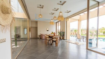 Ampla sala de estar com uma mesa de jantar, cadeiras e uma grande janela com vista para uma piscina.