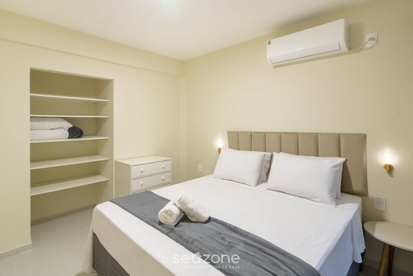 Quarto com cama, guarda-roupa, mesa de cabeceira e ar condicionado.