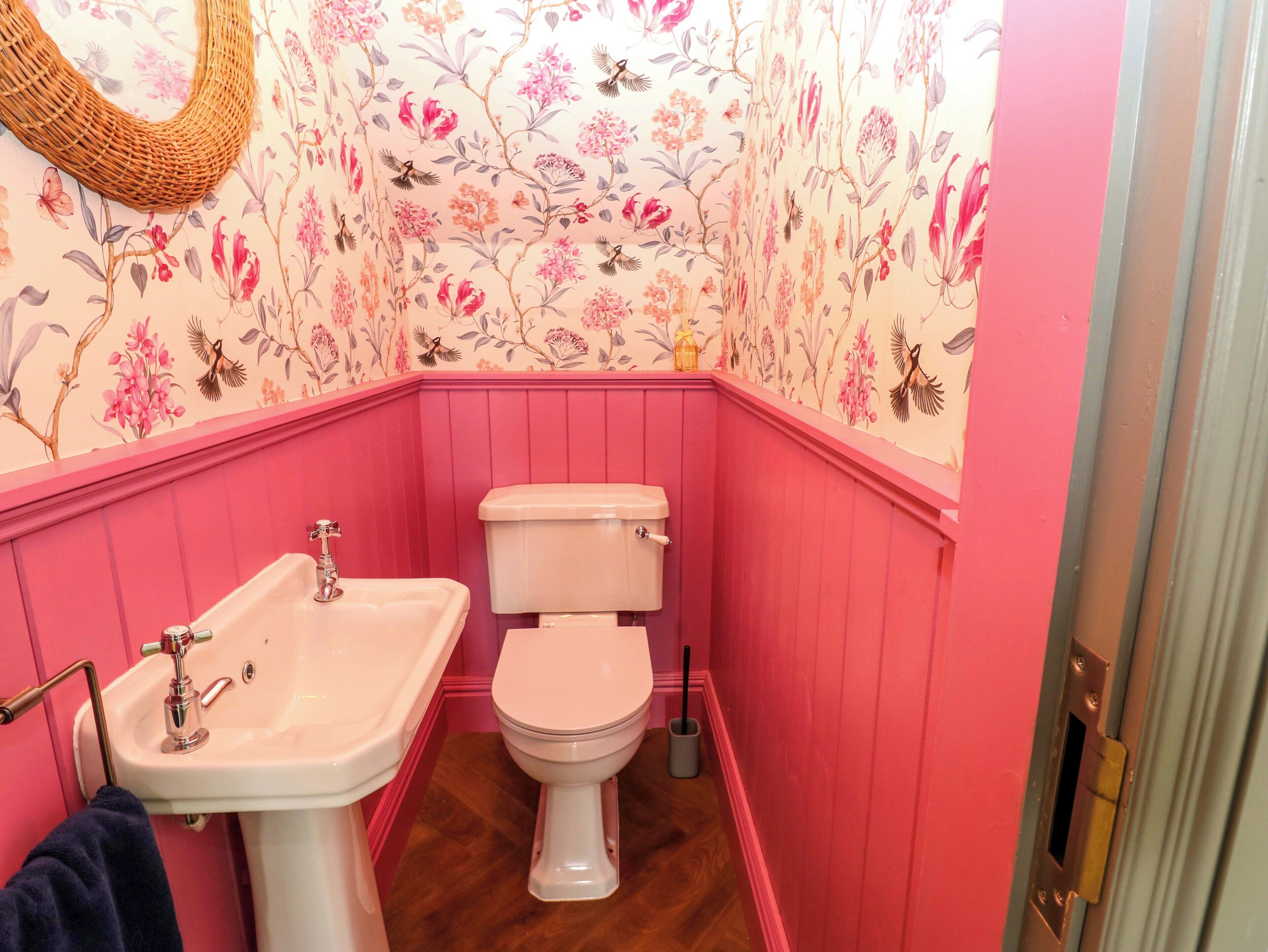 Casa de banho com paredes cor-de-rosa, sanita branca e lavatório com espelho.