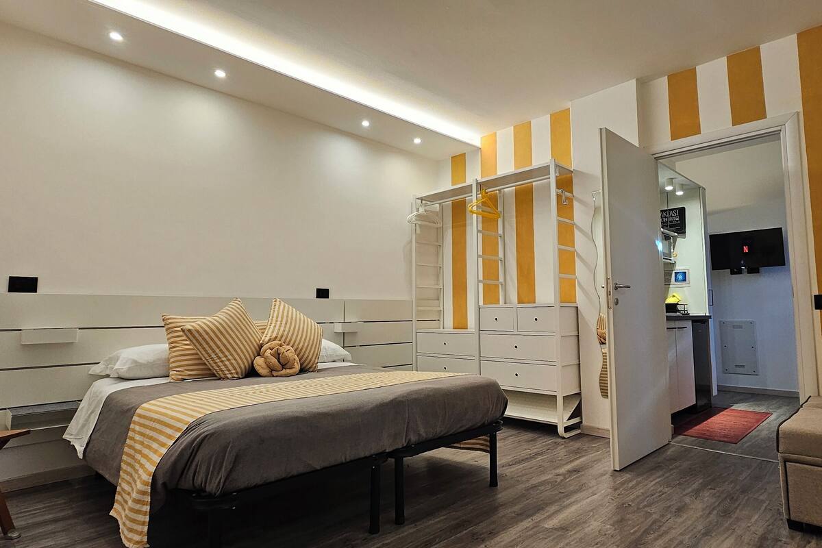 Quarto moderno com cama, mesas de cabeceira, guarda-roupa e um espaço de estar.