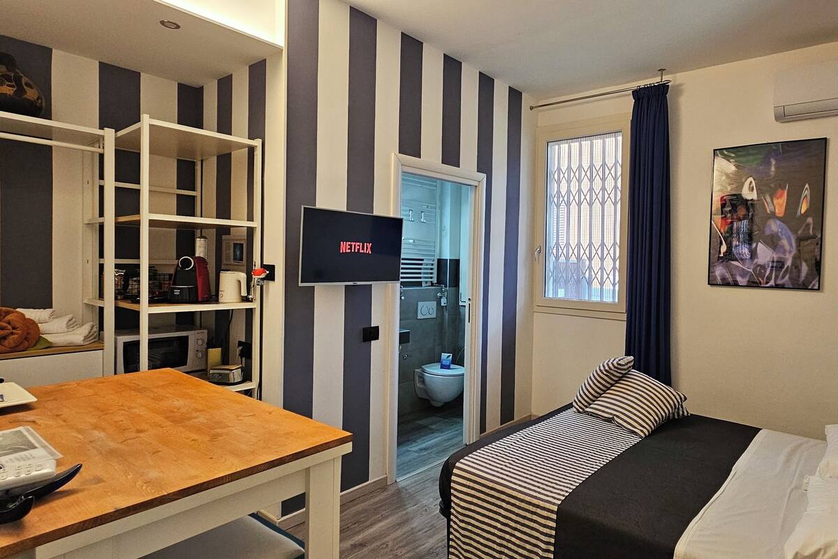 Quarto de hotel com cama, televisão, secretária e casa de banho visível através de uma porta aberta.