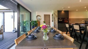 Uma área de refeições moderna com uma mesa comprida, cadeiras pretas e um vaso com flores.