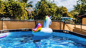 Piscina com bóia de unicórnio e palmeiras ao fundo.
