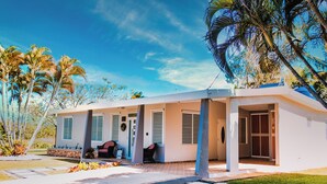 Uma casa moderna com varanda coberta, um pequeno jardim e palmeiras.
