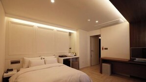 Quarto de hotel com uma cama grande, uma escrivaninha com cadeira, televisão e guarda-roupa.