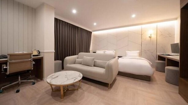 Quarto de hotel moderno com sofá, cama, escrivaninha e mesa redonda pequena.