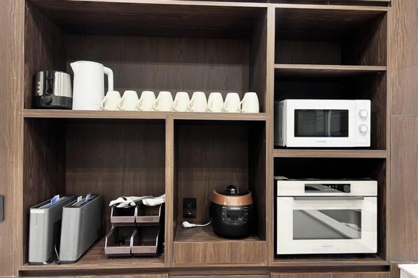Cozinha com micro-ondas, torradeira, chaleira e cafeteira nas prateleiras.