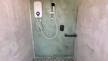 Um espaço de duche pequeno e fechado, com chuveiro manual, dispensador de sabonete e um prateleira pequena.