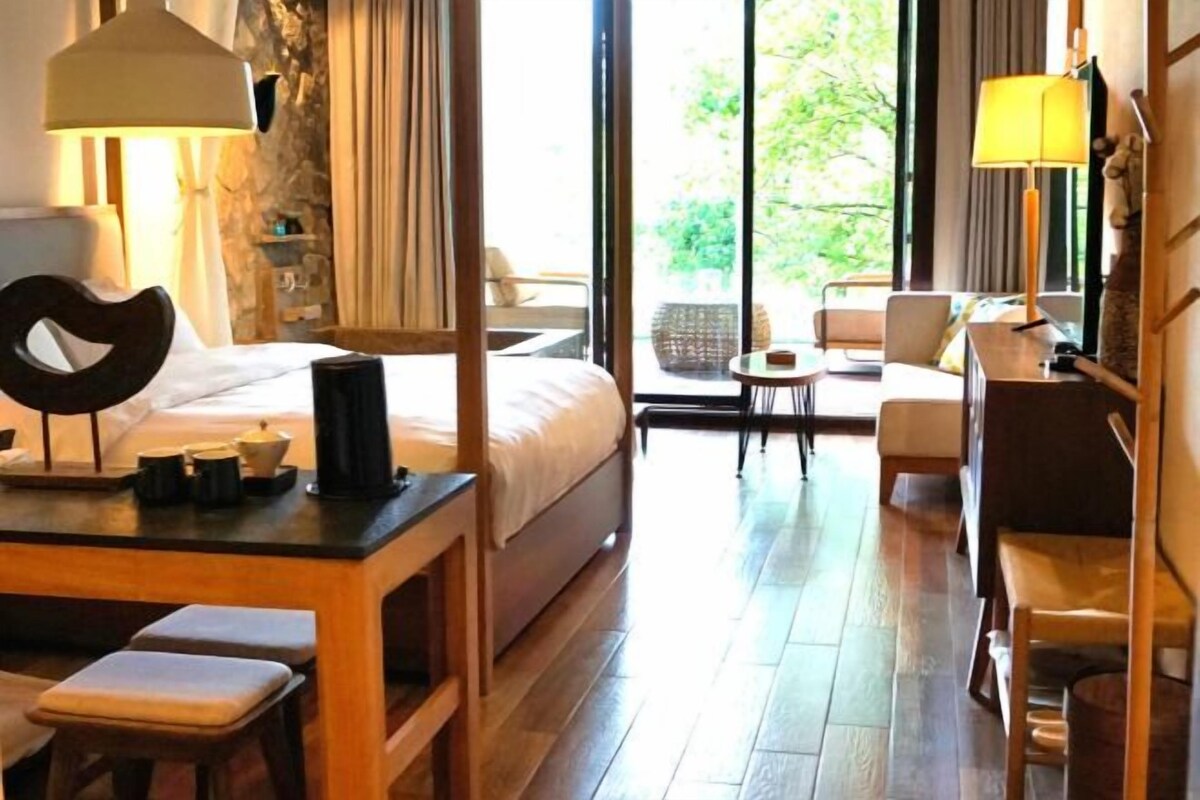 Quarto de hotel com cama, escrivaninha, cadeira e mesa pequena.