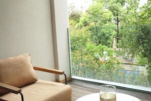 Quarto com vista para árvores pela janela, uma cadeira e um copo de água sobre uma mesa.