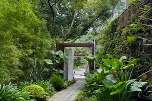 Caminho no jardim que leva a um arco de madeira, cercado por vegetação exuberante.