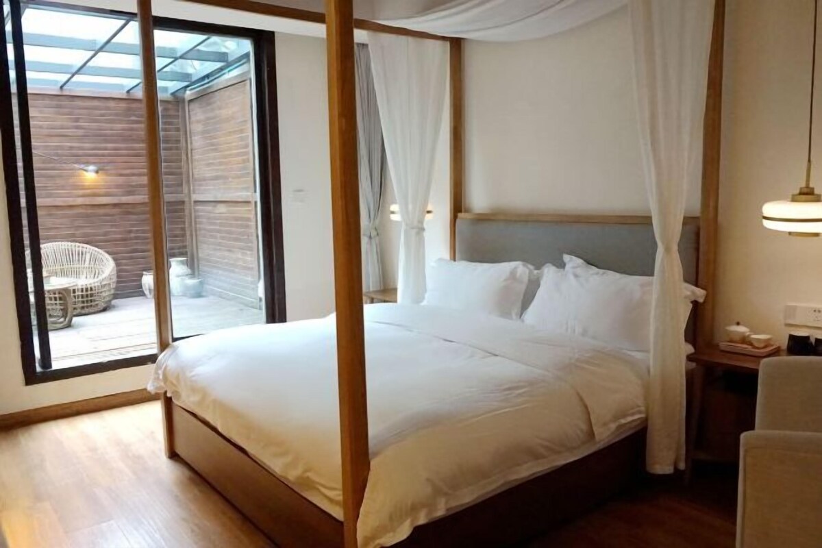 Quarto com cama de dossel, mesa de cabeceira e vista para um deck de madeira.