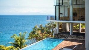 Um edifício moderno com varanda de vidro que dá para uma piscina e o oceano.