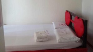 Uma cama de solteiro com cabeceira e peseira vermelhas, roupa de cama branca e duas almofadas vermelhas.