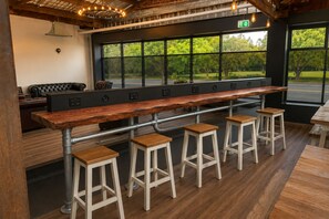 Um espaço de bar com um balcão comprido e quatro banquetas, um sofá de couro e vista para o exterior através de grandes janelas.