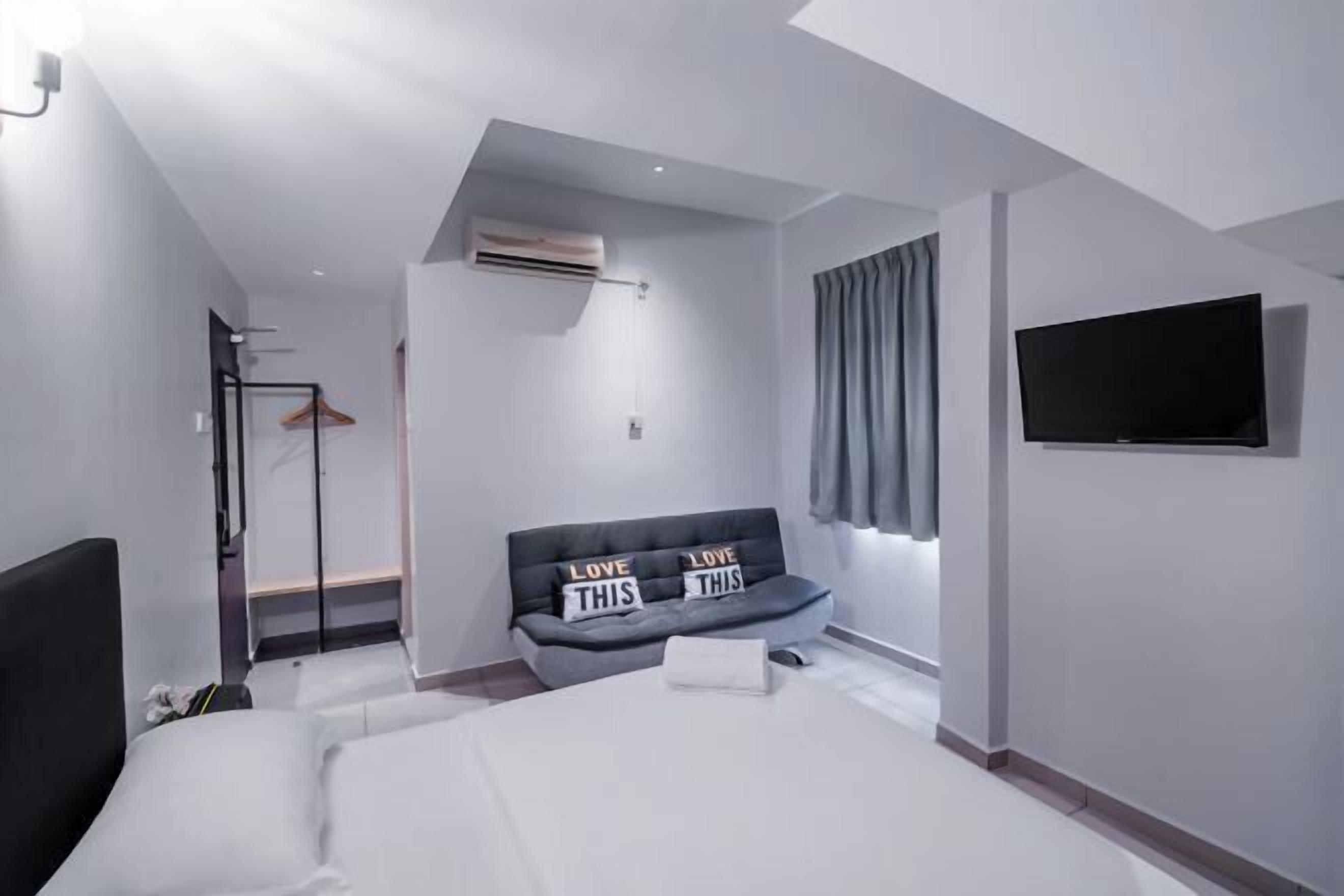 Quarto de hotel moderno com uma cama, um sofá com almofadas motivacionais, uma TV de tela plana e um ar condicionado.