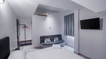 Quarto de hotel moderno com uma cama, um sofá com almofadas motivacionais, uma TV de tela plana e um ar condicionado.