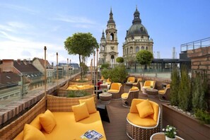Terraço no telhado com móveis de vime e vista para um edifício histórico.