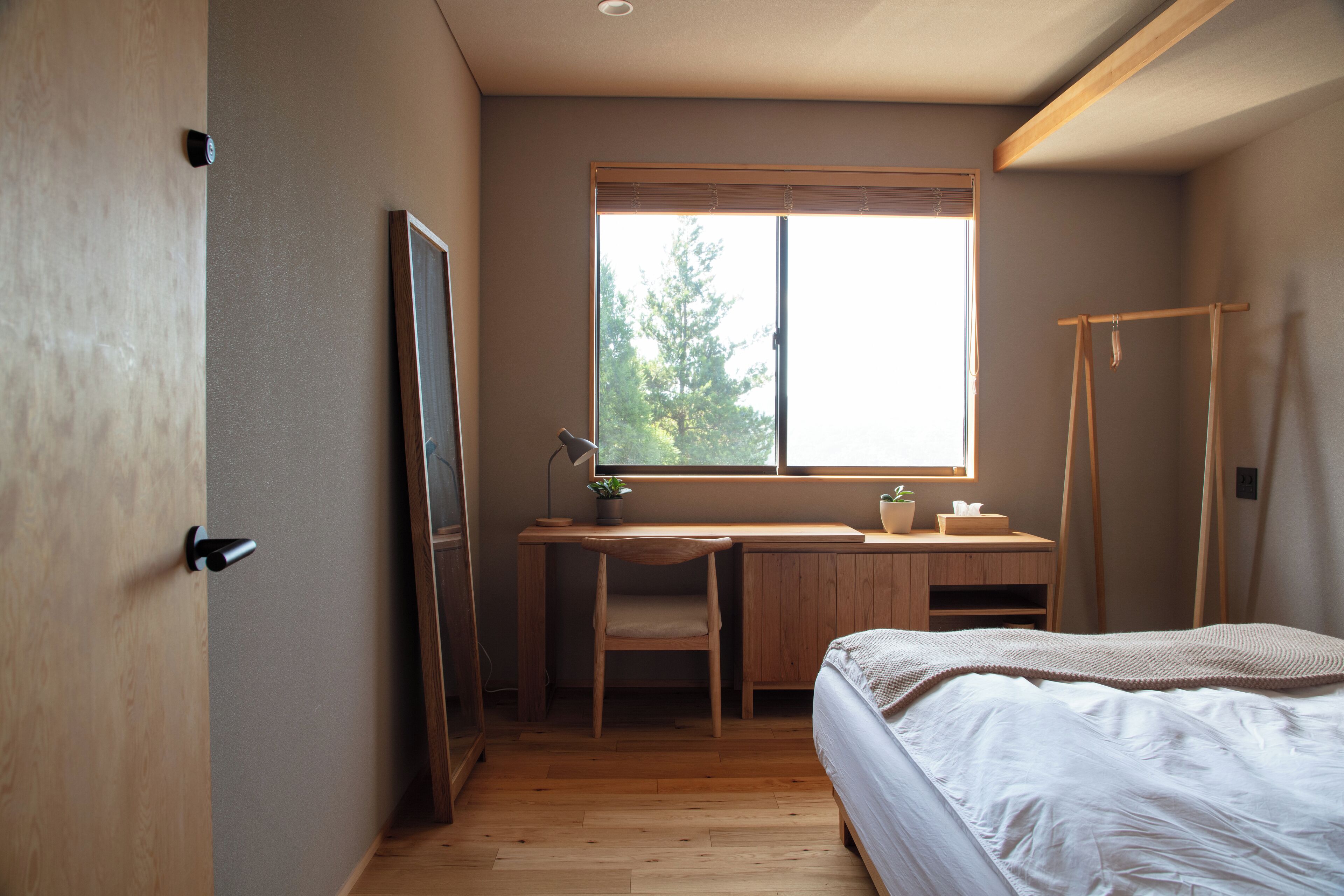 Quarto com cama, escrivaninha, cadeira e janela com persianas.