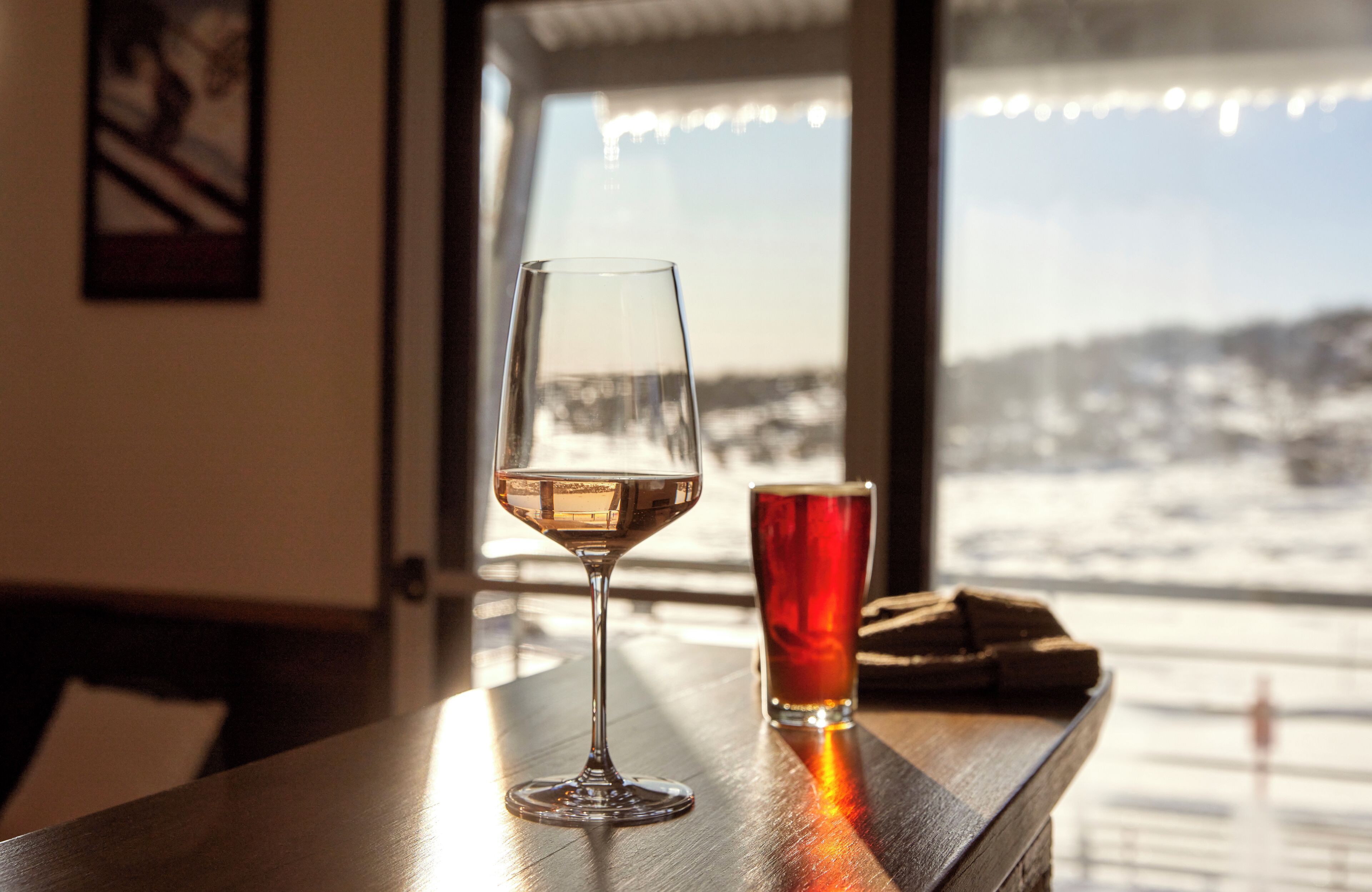 Um copo de vinho branco e um copo de vinho tinto sobre uma mesa de madeira, perto de uma janela com vista para uma paisagem nevada.