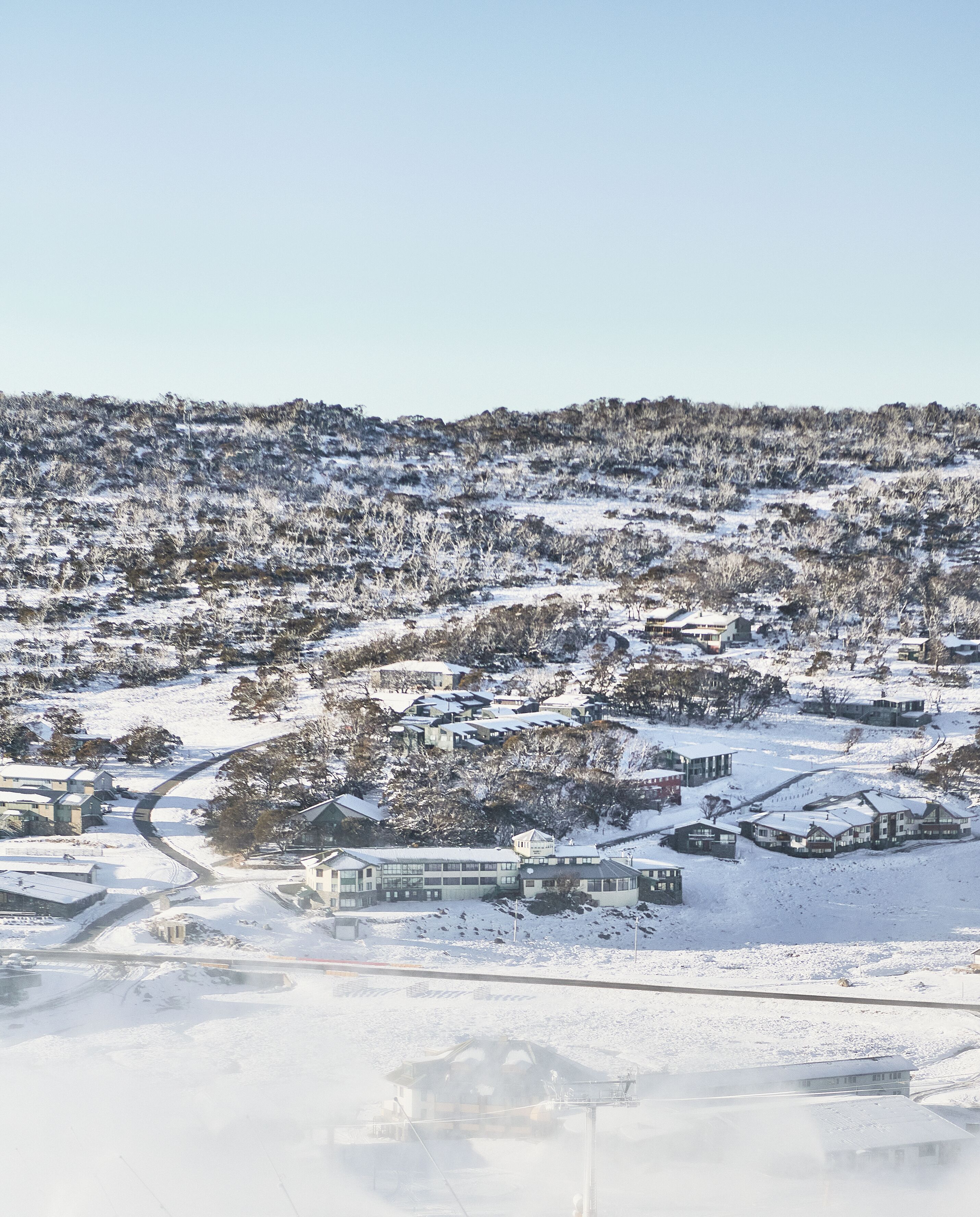 Paisagem coberta de neve com um conjunto de edifícios, incluindo um hotel grande com várias divisões e uma construção menor nas proximidades.