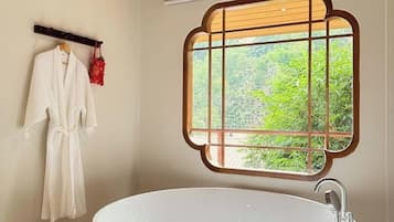 Casa de banho com banheira, janela com moldura de madeira e roupão pendurado num porta-roupões.