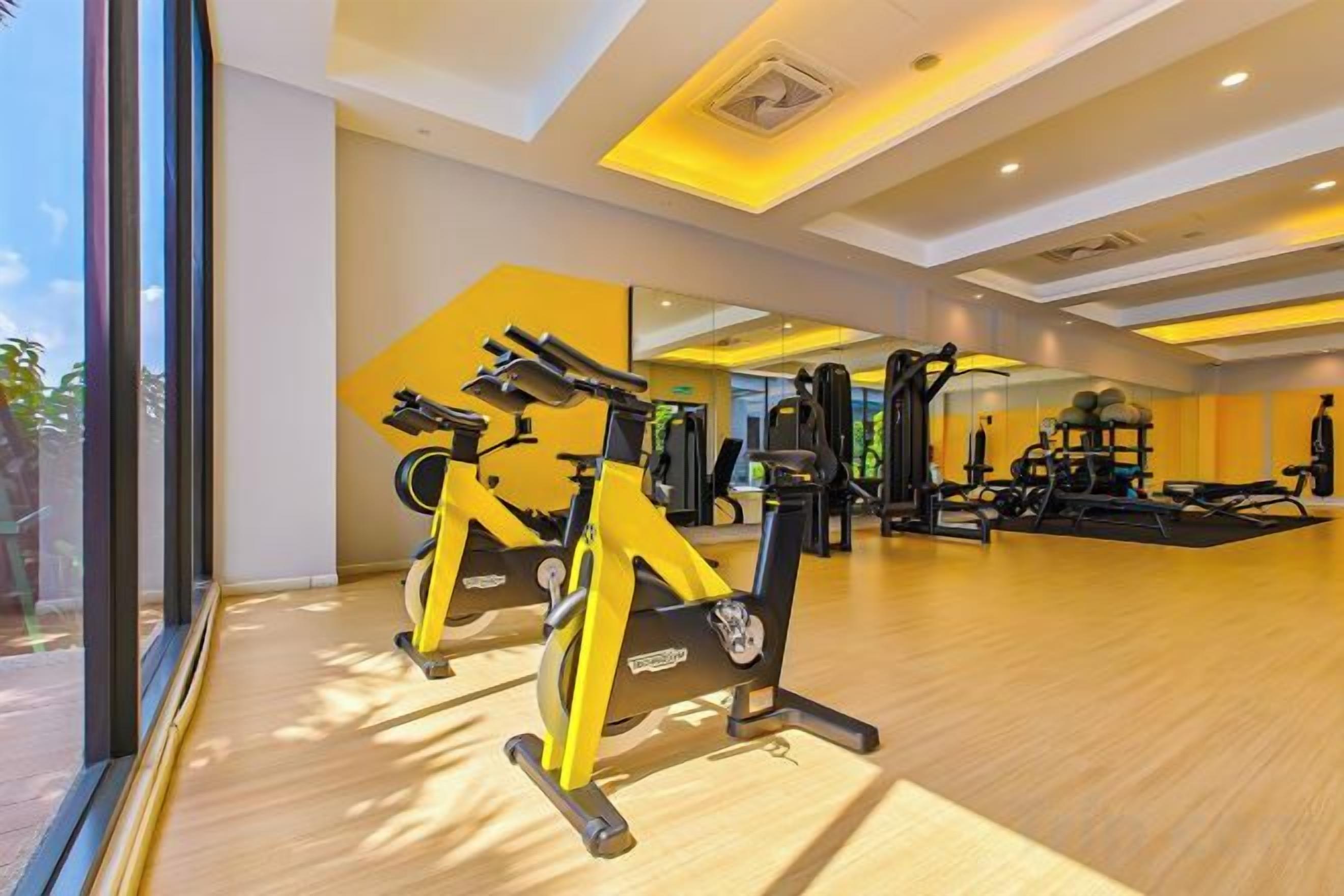 Academia com bicicletas ergométricas, aparelhos de musculação e um grande espelho.