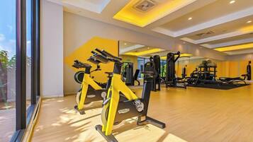 Academia com bicicletas ergométricas, aparelhos de musculação e um grande espelho.