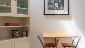 Quarto com um armário branco, uma fotografia a preto e branco emoldurada e uma mesa de madeira com duas cadeiras.