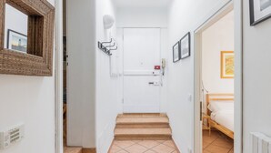 Um corredor estreito com escada que leva a um quarto. O quarto possui uma cama, uma mesinha de cabeceira e um aplique na parede.