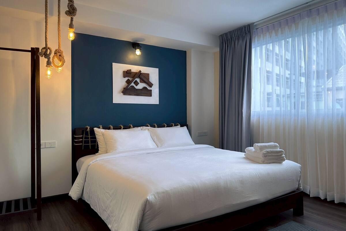 Cama bem arrumada com roupa de cama branca, cabeceira com design de madeira e quadro na parede.