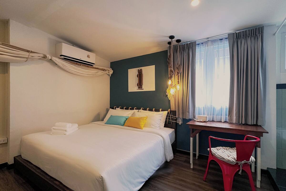 Quarto de hotel com uma cama, uma escrivaninha e uma cadeira.