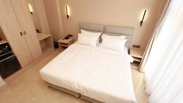Quarto de hotel com uma cama grande, um guarda-roupa, uma mesa de cabeceira e uma mesinha de apoio.
