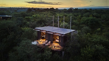 Uma cabana isolada com varanda, rodeada por uma floresta densa.