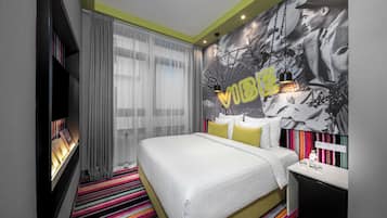 Quarto de hotel moderno com uma cama grande, estante de livros, tapete listrado colorido e um mural na parede.