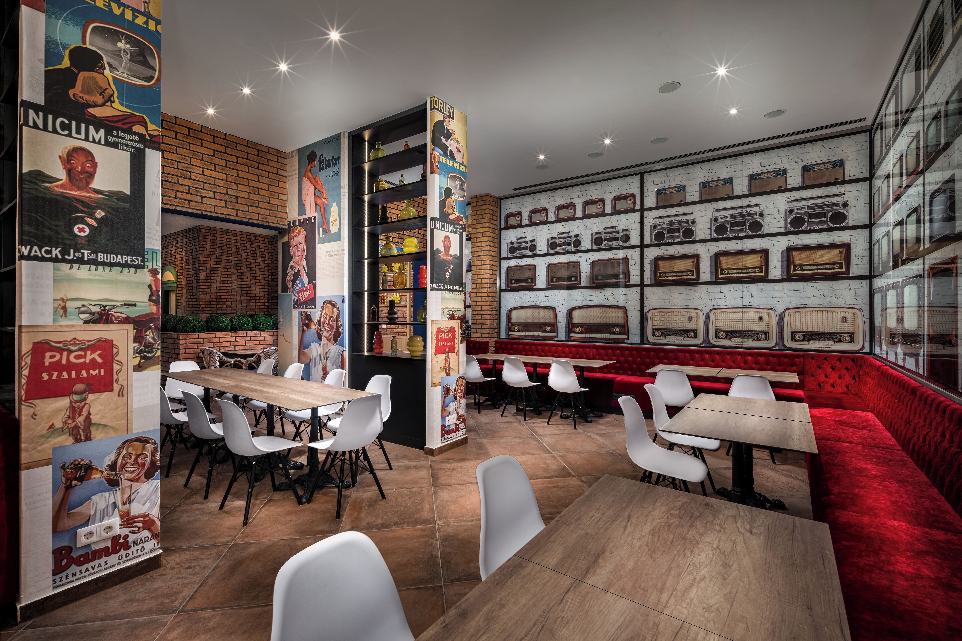 Interior de restaurante com tem ática retrô, paredes de tijolo, pôsteres antigos e área de assentos com almofadas vermelhas.