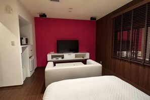 Quarto de hotel com cama, televisão, secretária branca e parede vermelha.