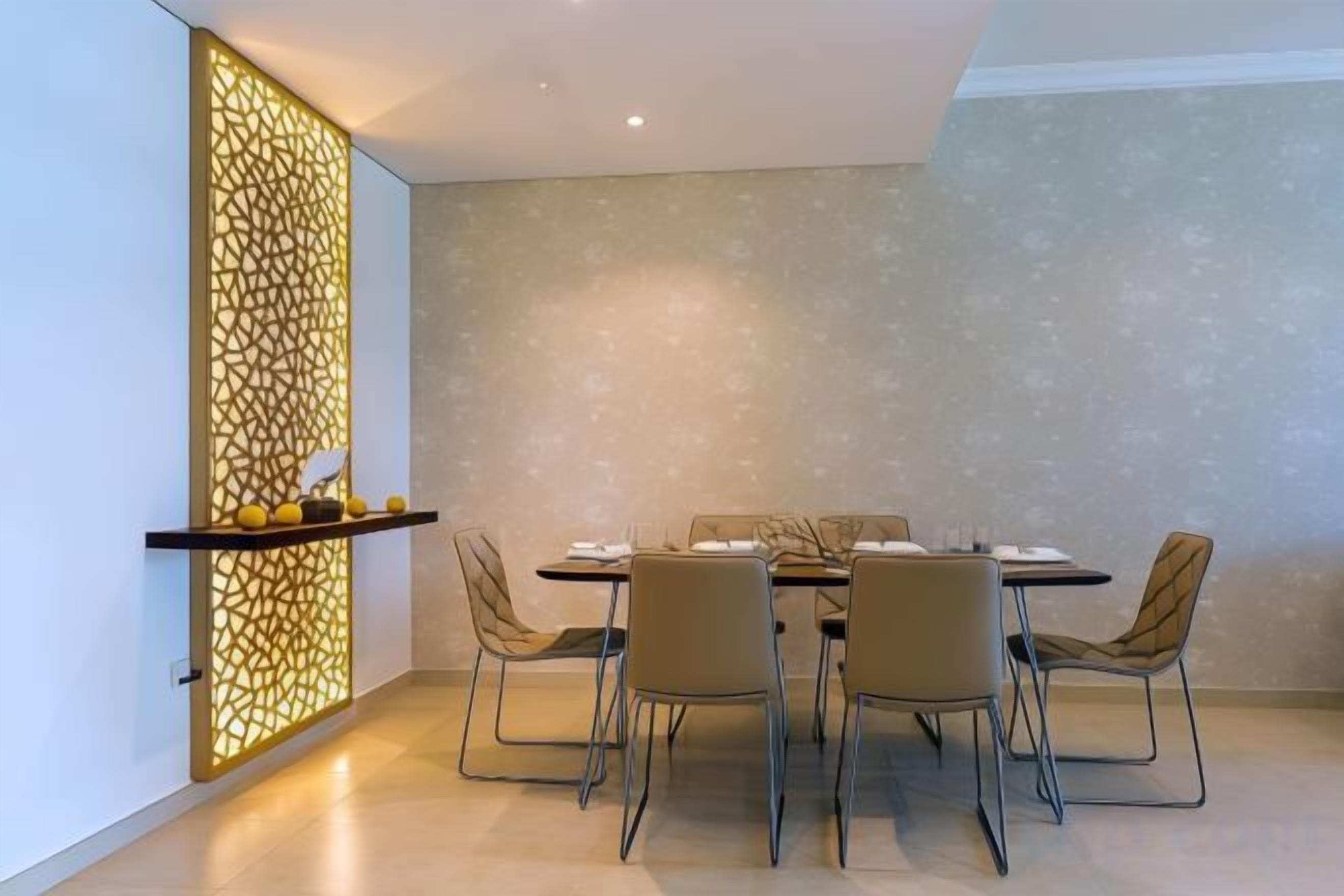 Uma área de refeições com uma mesa posta para quatro pessoas, rodeada por cadeiras, e um separador decorativo com padrão geométrico.