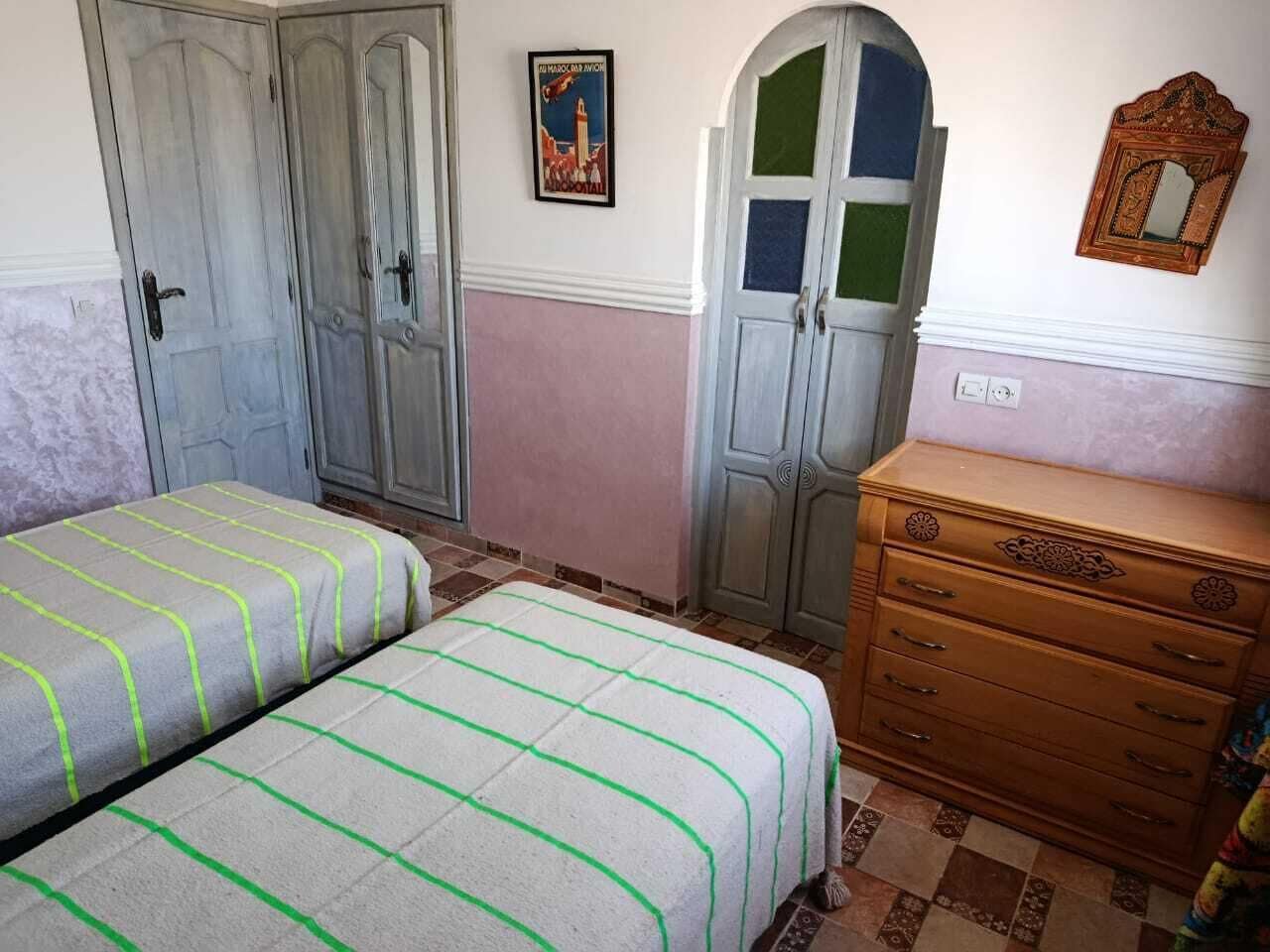 Quarto com duas camas, uma cômoda e uma porta com um pôster na parede.