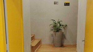 Uma escadaria leva a um quarto com uma planta em vaso, uma porta com moldura amarela e uma placa na parede.