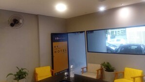 Uma área de recepção com balcão, duas cadeiras amarelas, um ventilador, uma planta em vaso e um grande letreiro do Unity Hotel Alliance.