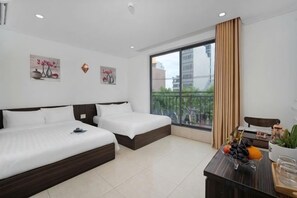 Quarto de hotel com duas camas, uma janela ampla e vista, uma escrivaninha com um vaso e uma planta.
