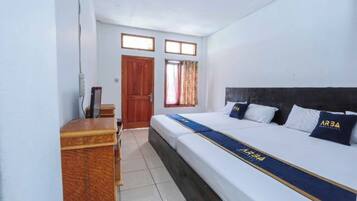 Quarto de hotel com cama, escrivaninha de madeira, janela e porta.