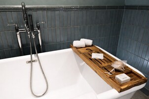 Uma casa de banho moderna com banheira, um tabuleiro de madeira com artigos de higiene pessoal e um porta-toalhas.