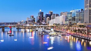 Silhueta urbana com edifícios modernos, uma ponte e uma orla marítima com barcos.