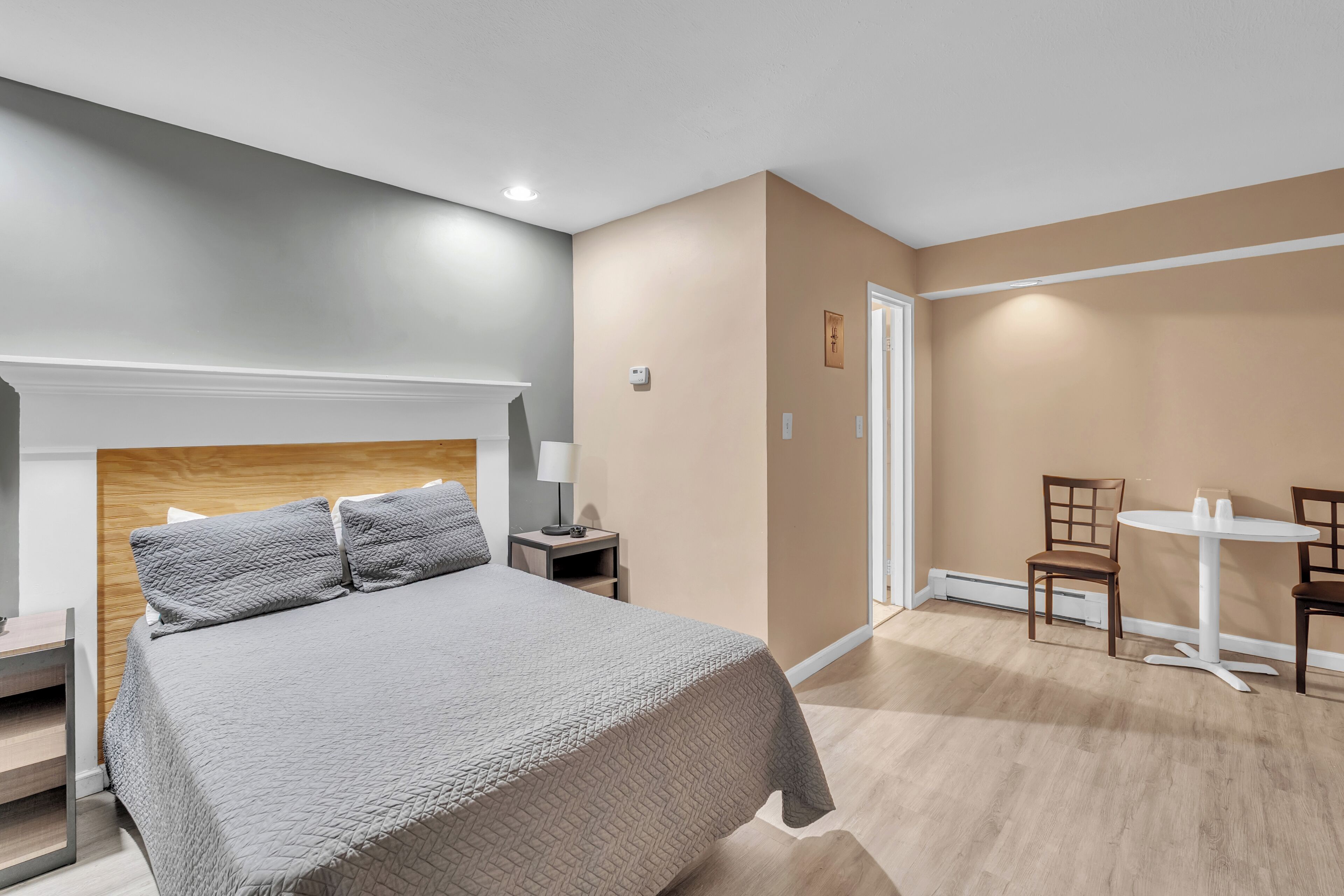 Quarto com cama, mesa de cabeceira, luminária e uma pequena mesa com cadeiras.