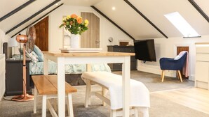 Um quarto de sótão aconchegante com teto inclinado, uma mesa de madeira, um banco, uma cama com roupa de cama floral, uma TV e uma cadeira.