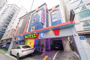 Um motel com letreiro de neon, estacionamento e um edifício com vários andares.