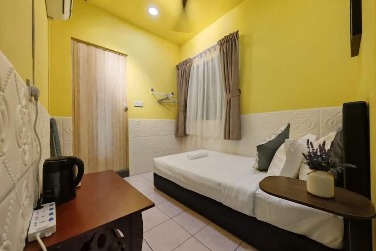 Quarto com cama, mesa de cabeceira com chaleira, tomada e janela com cortinas.