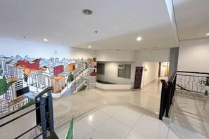 Um hall de hotel com design moderno, apresentando um grande mural, uma escadaria e um balcão de recepção.